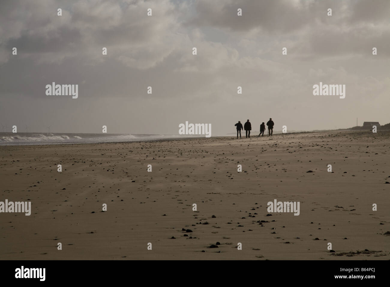 Four people walking along a deserted beach on the Norfolk coast in ...