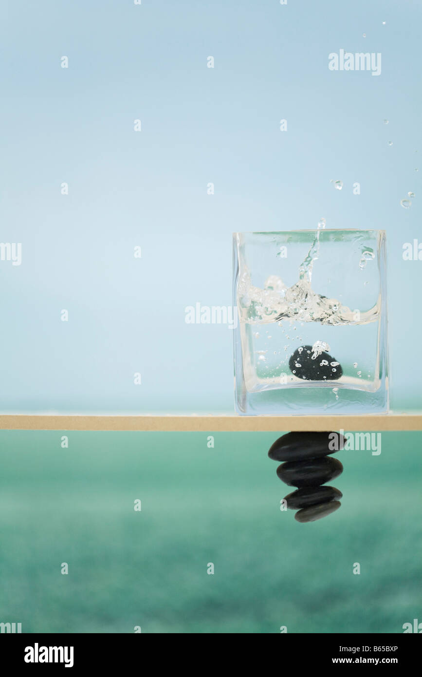Stone falling in glass container, creating water splash, pile of stones ...