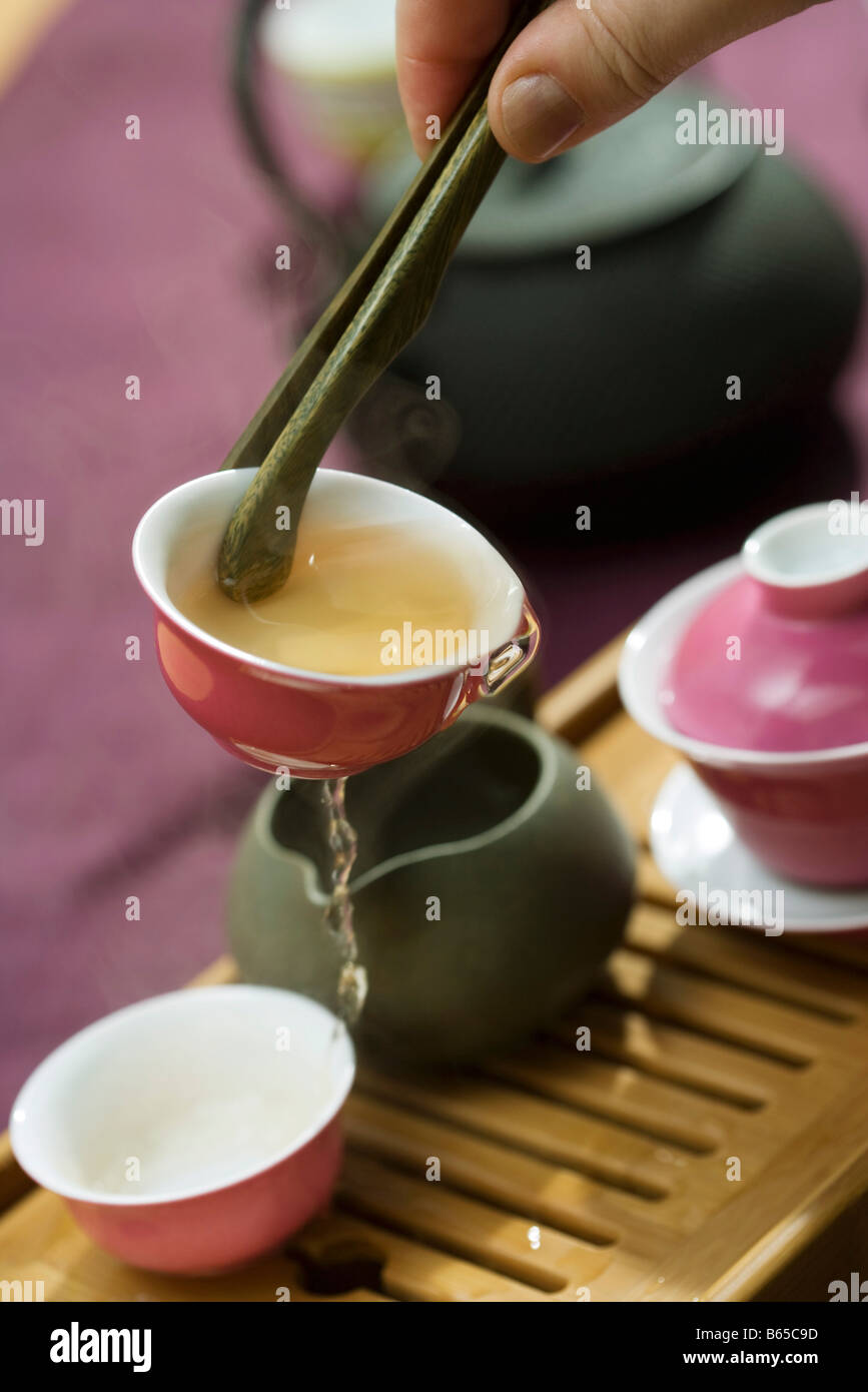 Tea cup held with tea tongs, pouring out first brew into tea tray Stock ...