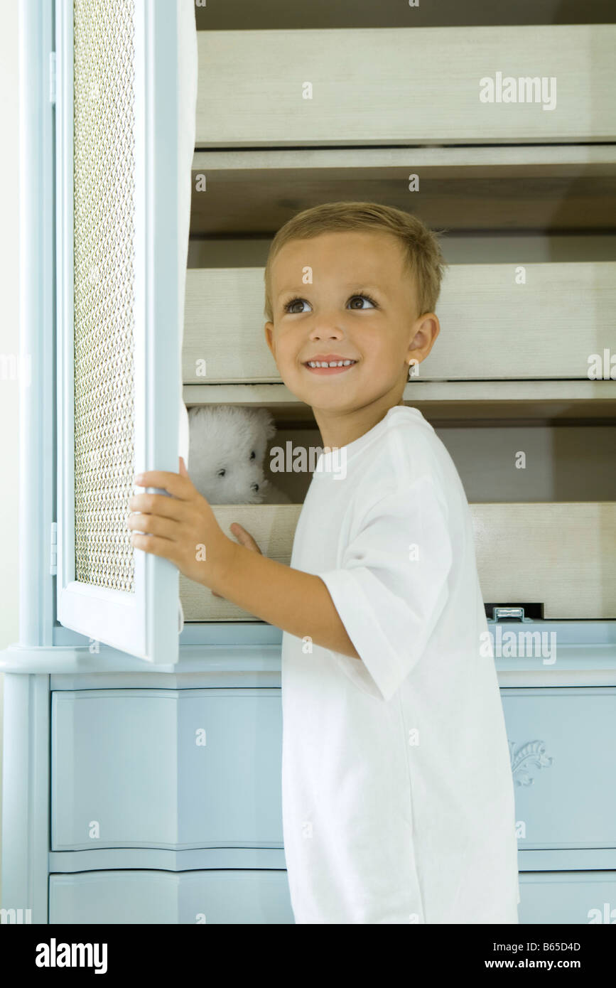 Boy opening cabinet, teddy bear inside Stock Photo - Alamy