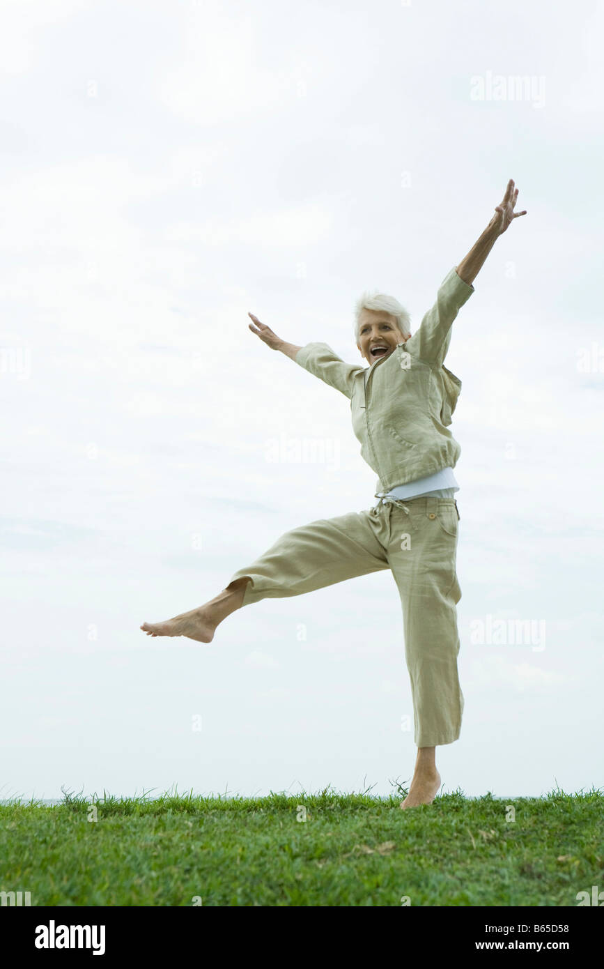 Senior woman standing on one leg outdoors, arms raised in the air Stock ...
