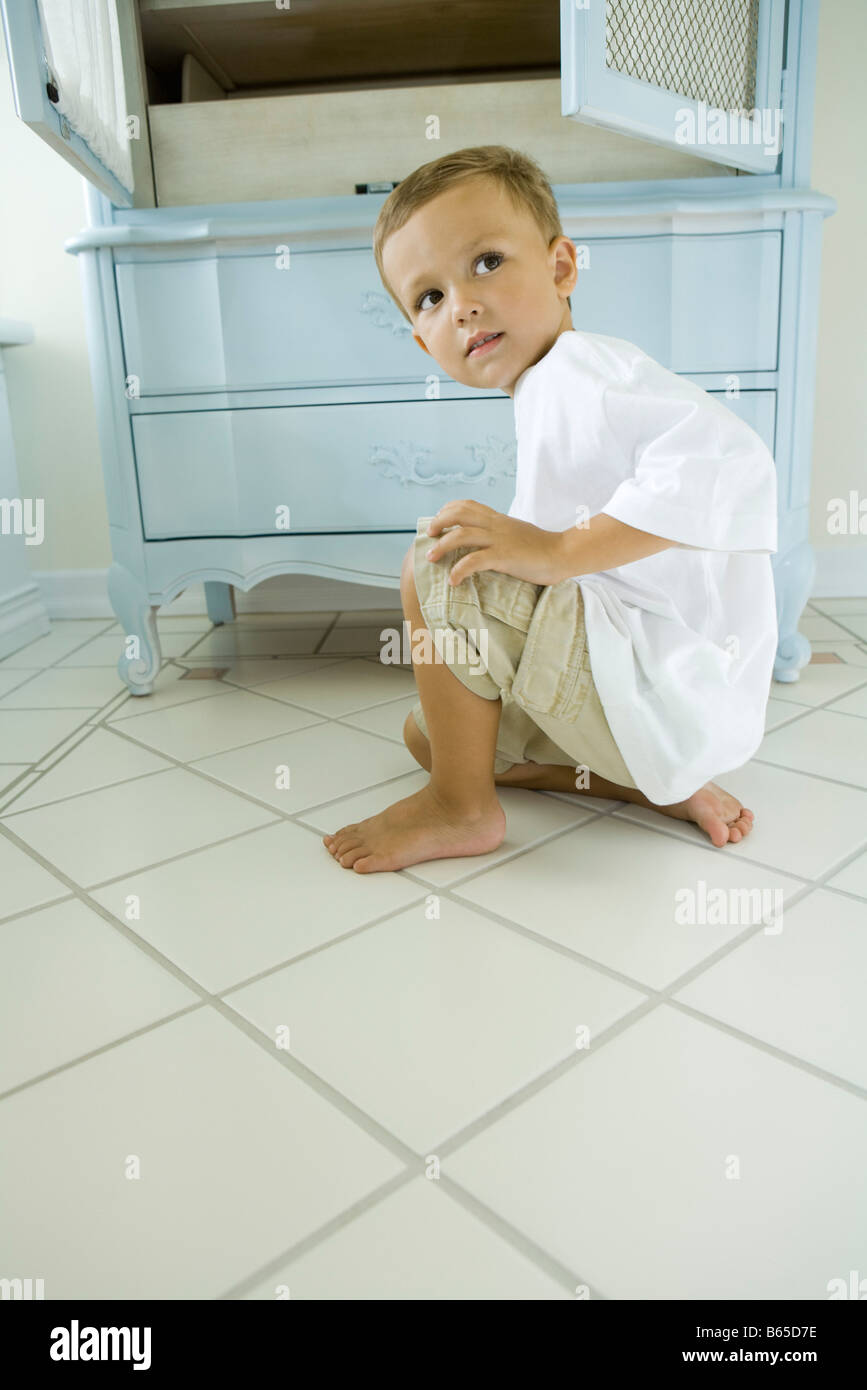 Boy crouching beside open armoire, looking over shoulder Stock Photo ...