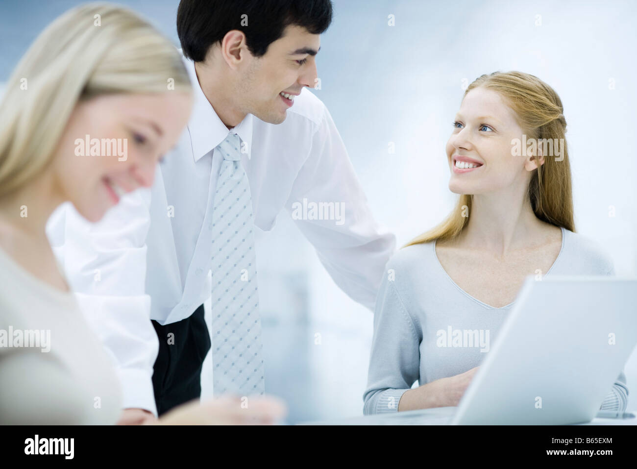 Businessman leaning over, chatting with female colleagues Stock Photo ...