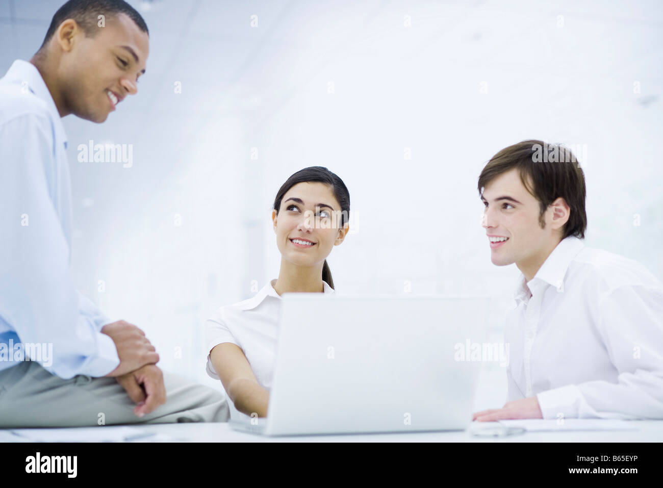 Young professionals sitting around laptop computer, smiling Stock Photo ...
