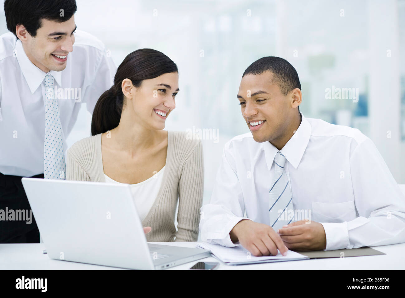 Young professionals sitting around laptop computer, smiling Stock Photo ...