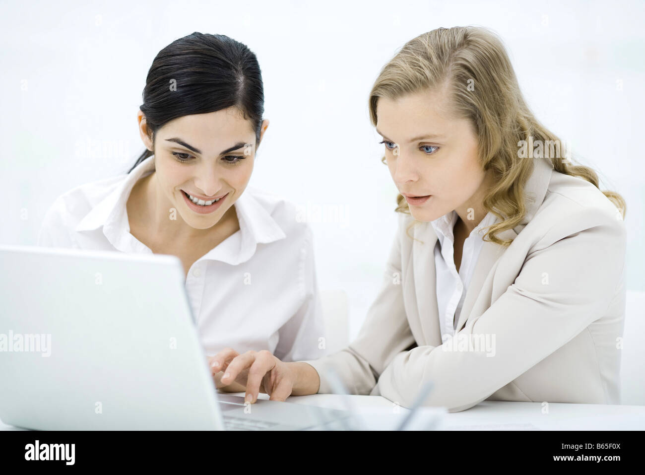 Professional women looking at laptop computer together, smiling Stock ...