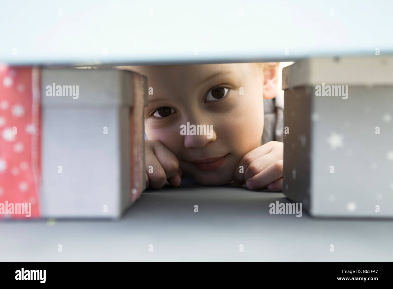 Little boy hiding behind pile of presents, peeking at camera Stock ...