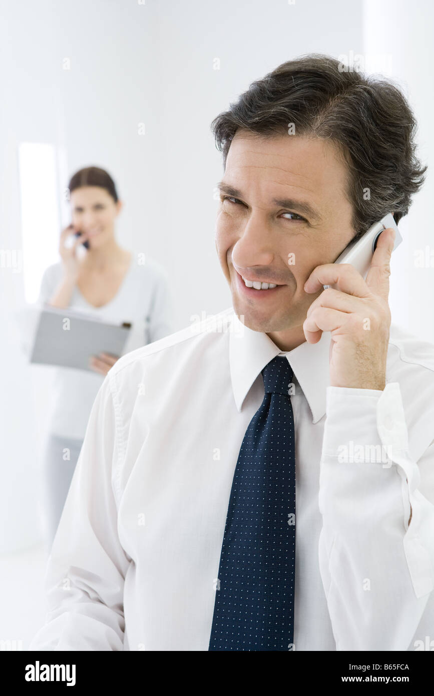 Professional man using cell phone, smiling at camera, woman on phone in ...