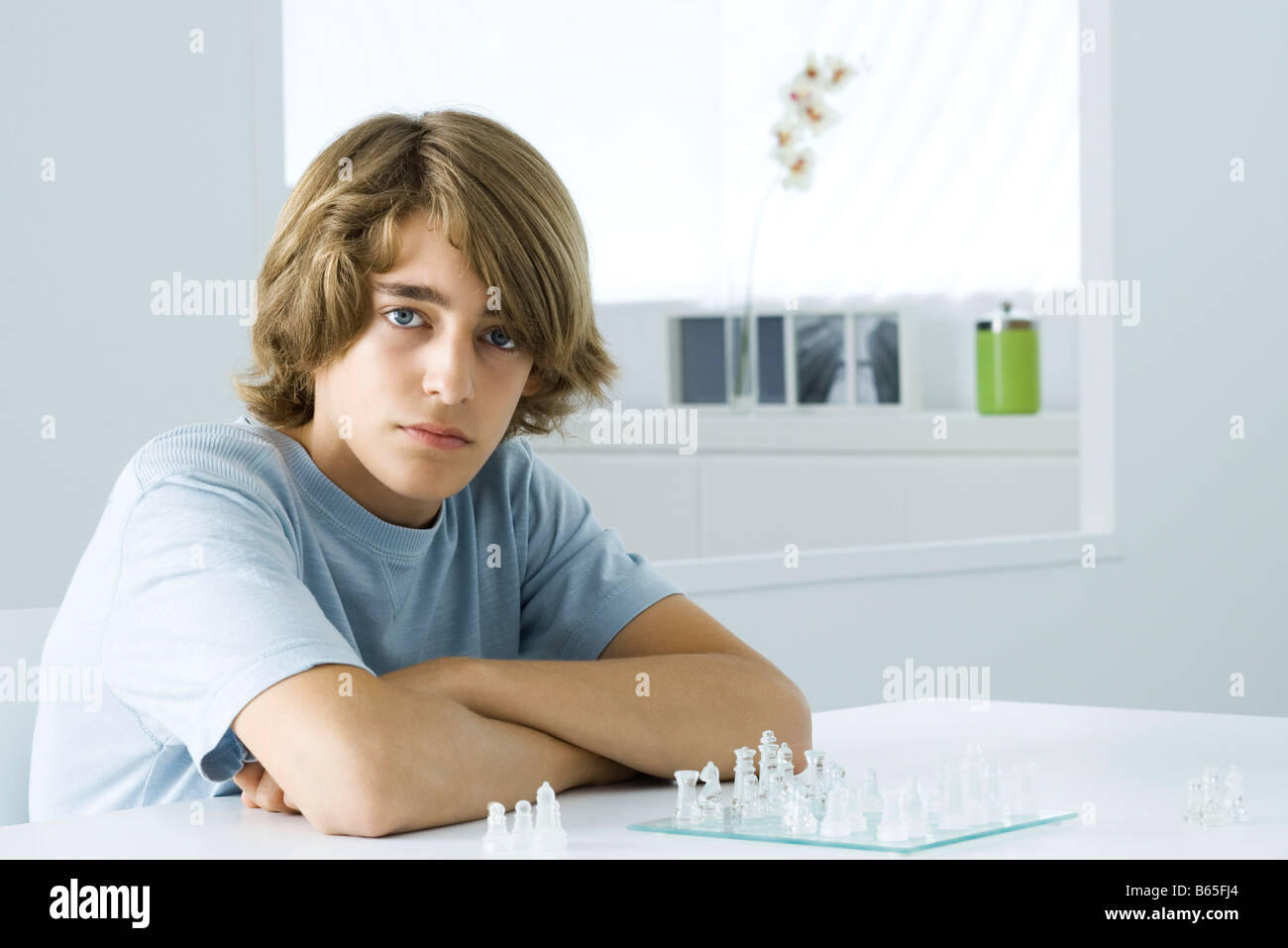 Teen boy sitting at table, playing chess, looking at camera Stock Photo ...
