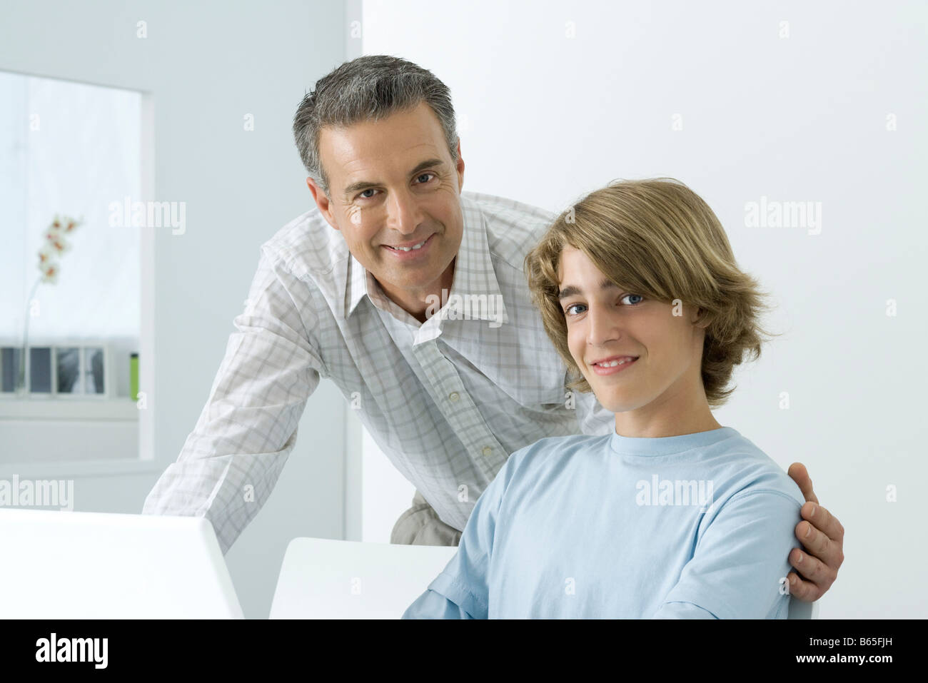 Father and son smiling at camera, man's arm around teenager's shoulder ...