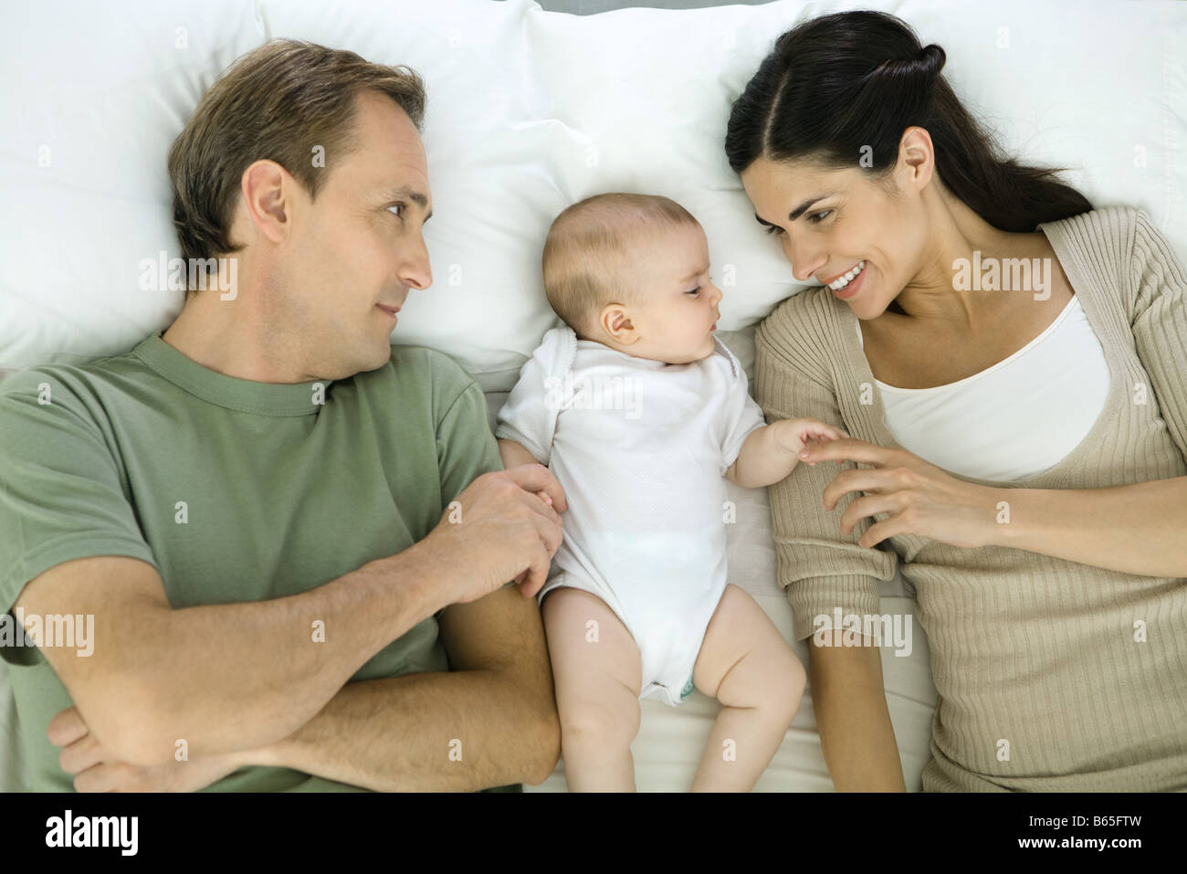 Family resting on bed, baby lying in between parents, overhead view ...
