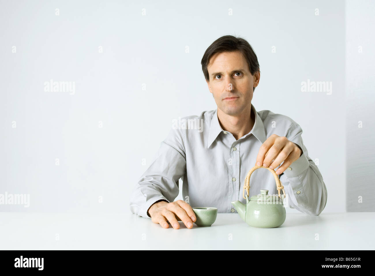 Man sitting with teapot and teacup, looking at camera Stock Photo - Alamy