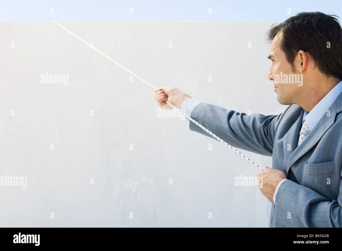 Businessman standing beside wall, pulling rope hanging over edge Stock ...