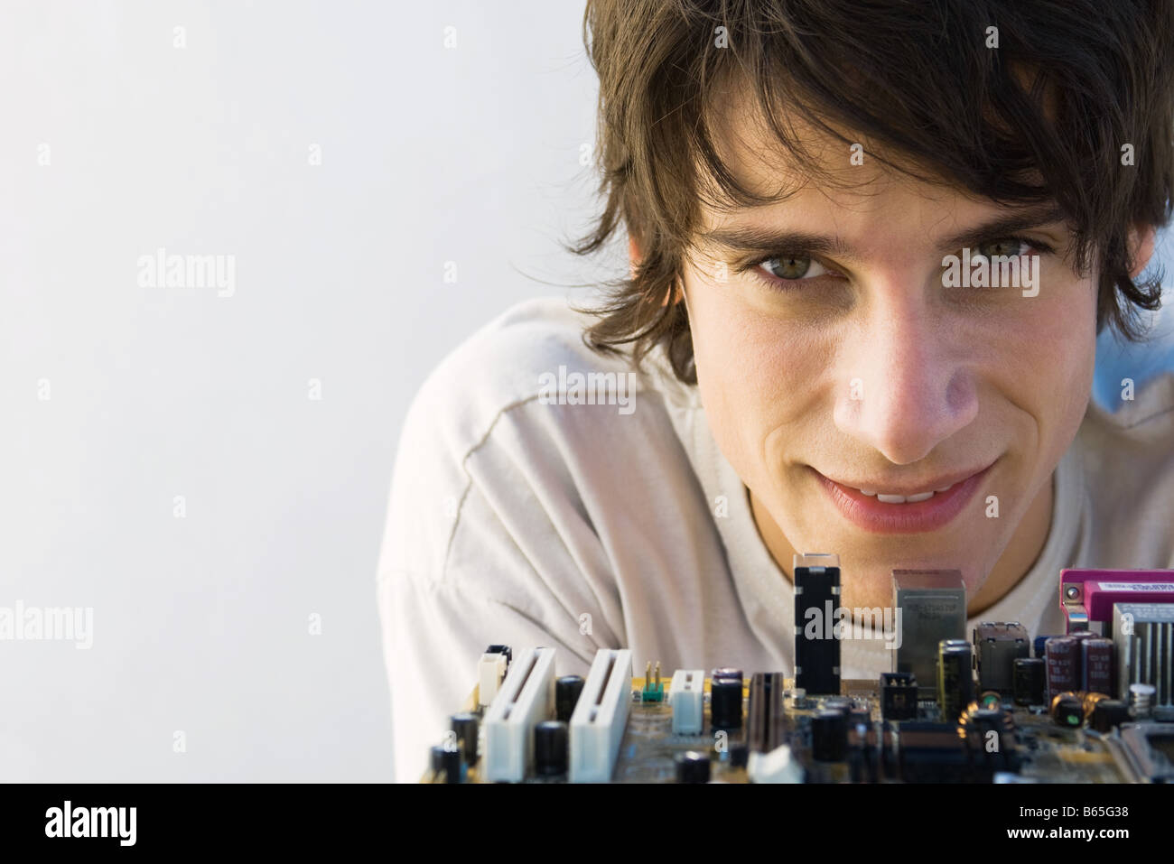Young man leaning over computer motherboard, smiling at camera Stock ...