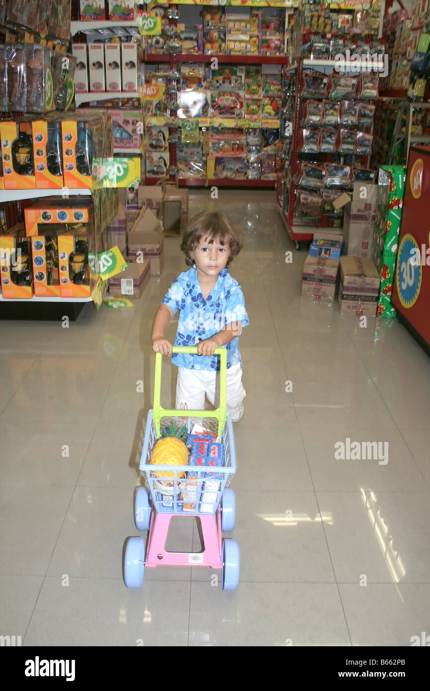 A young child in a toy store pushing a toy shopping cart Stock Photo ...