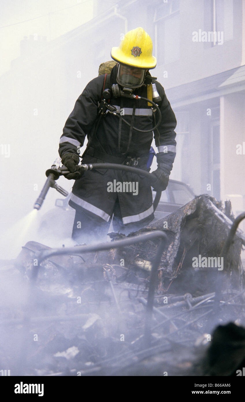 UK British Fireman putting out car fire in street wearing breathing ...