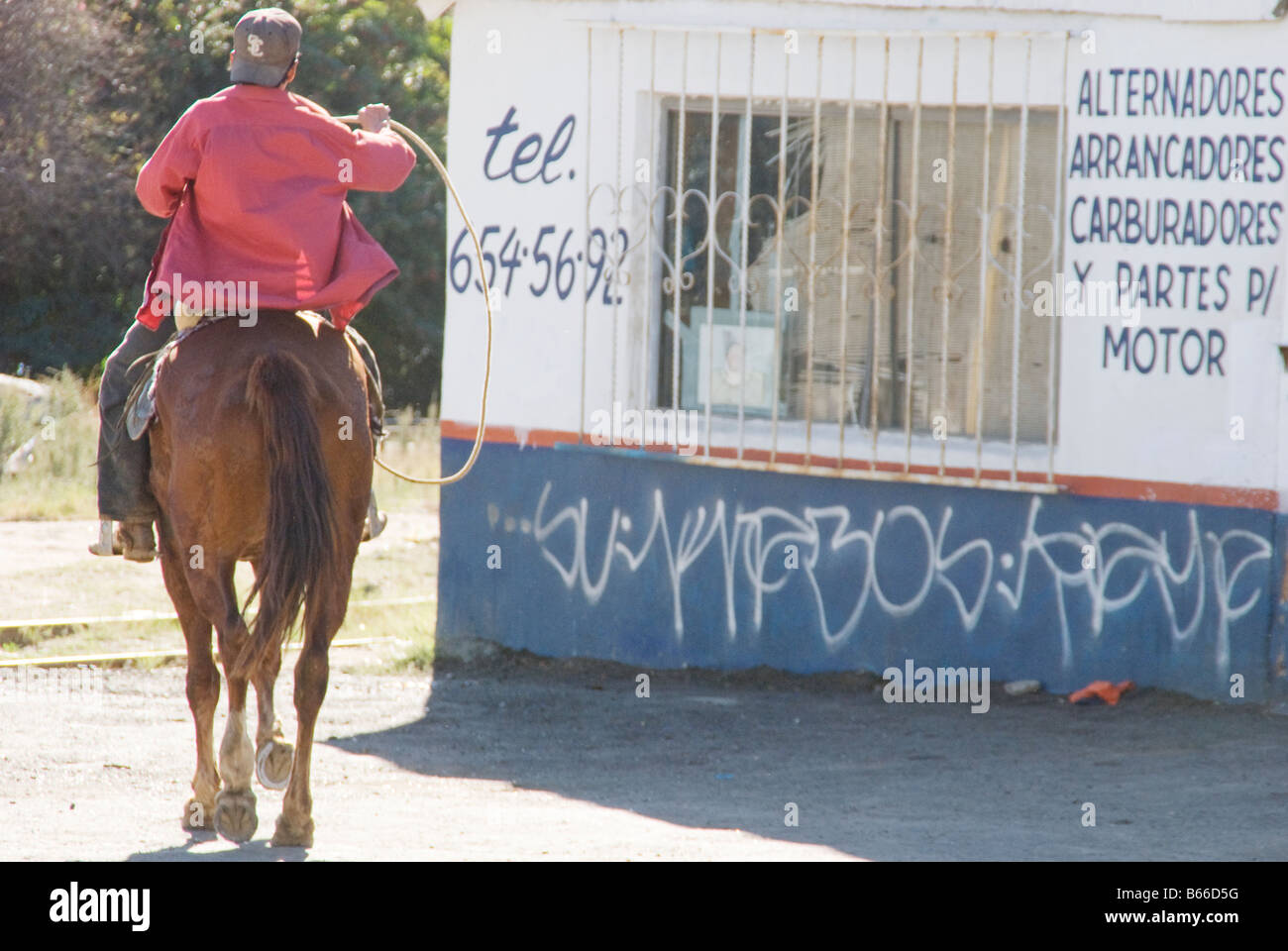 A man on horseback trots past a garage on a street in Tecate Mexico ...