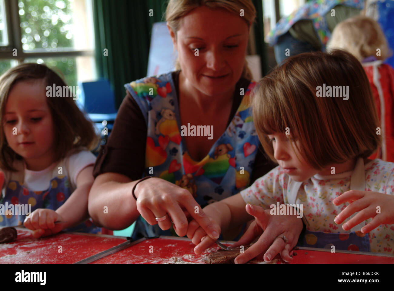 Woman helping children make chocolate biscuits cookies at nursery Stock ...