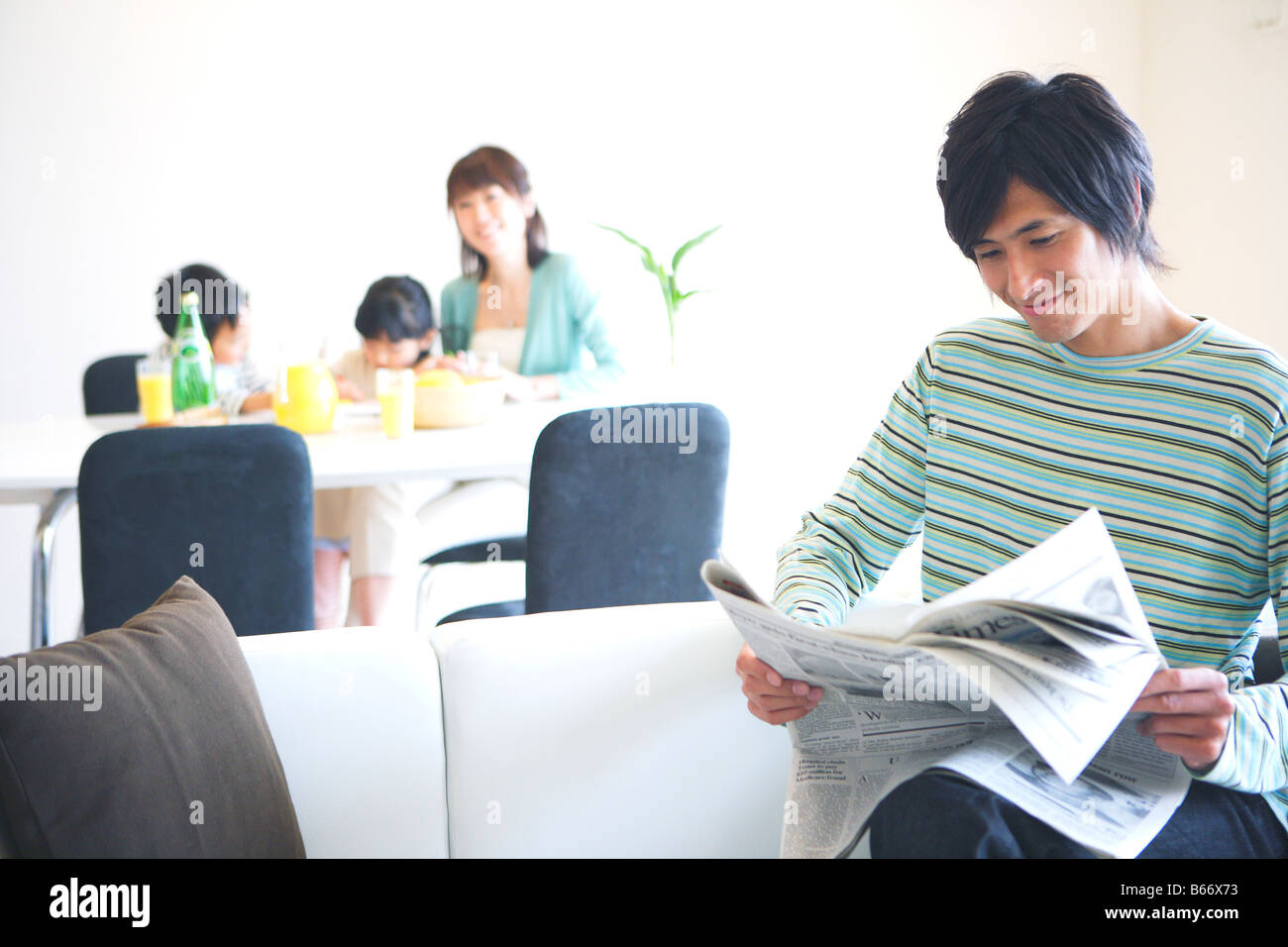 Father Reading Newspaper on Sofa, Mother and Children in Background ...