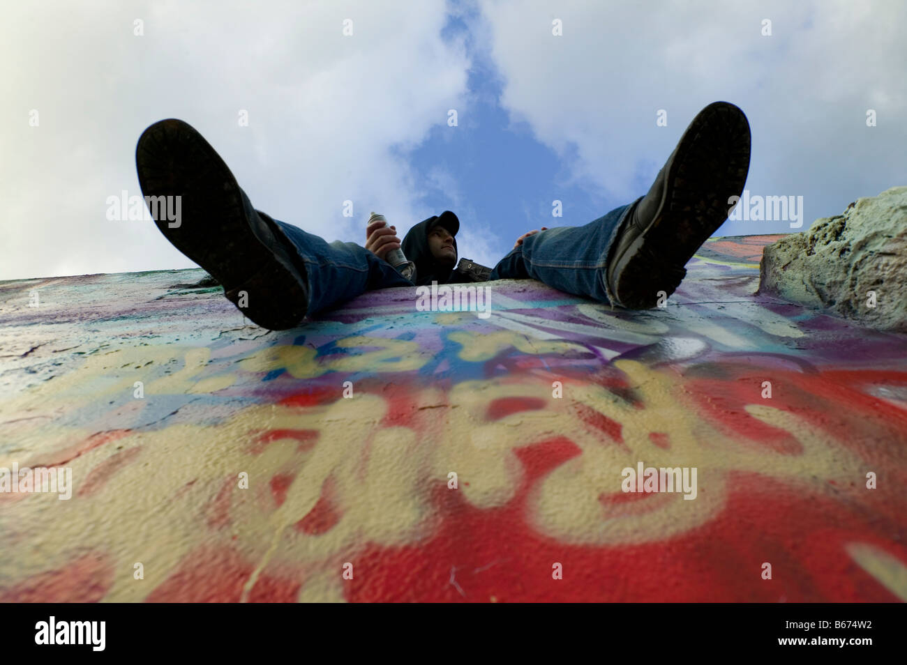 Graffiti artist sits above a painted wall Stock Photo - Alamy