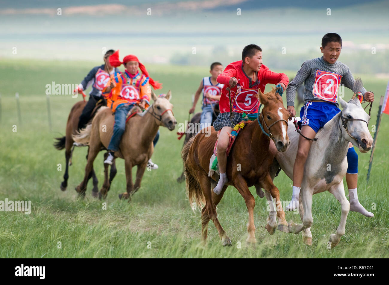 Ethnic Mongolian costumed boy jockeys race horses at summertime Naadam ...