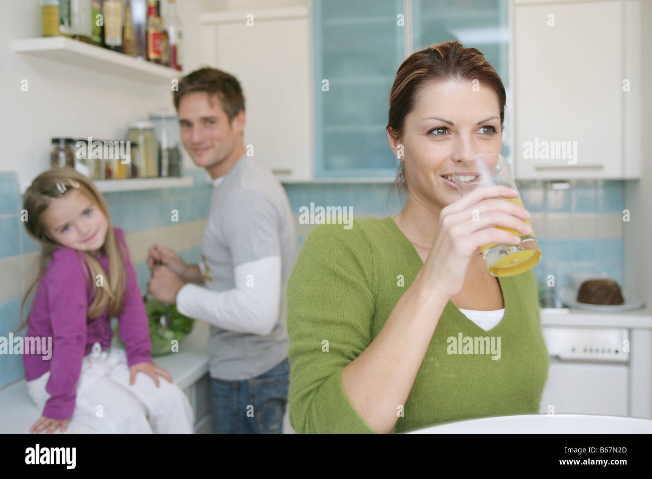 Young woman drinking a glas of juice, man and daughter in background ...
