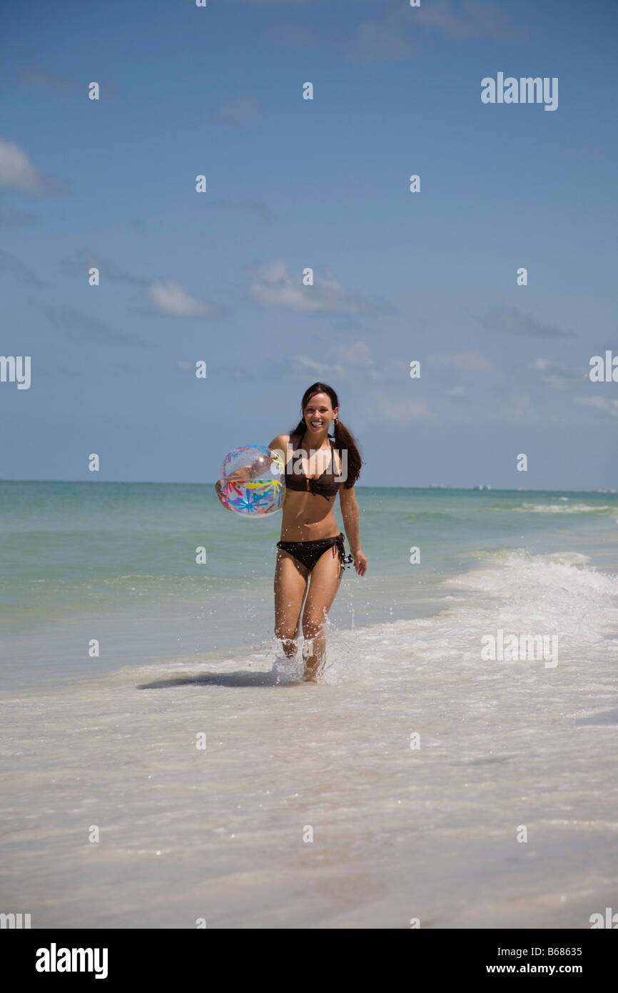 Woman with ball running along beach Stock Photo - Alamy