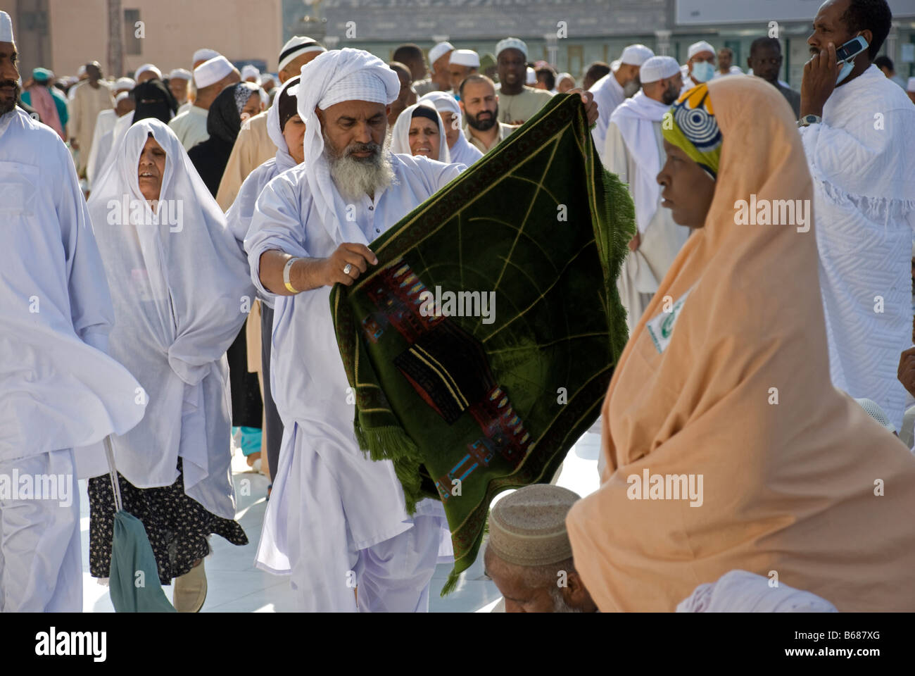 A muslim pilgrim opening his prayer mat to be put on the floor outside ...