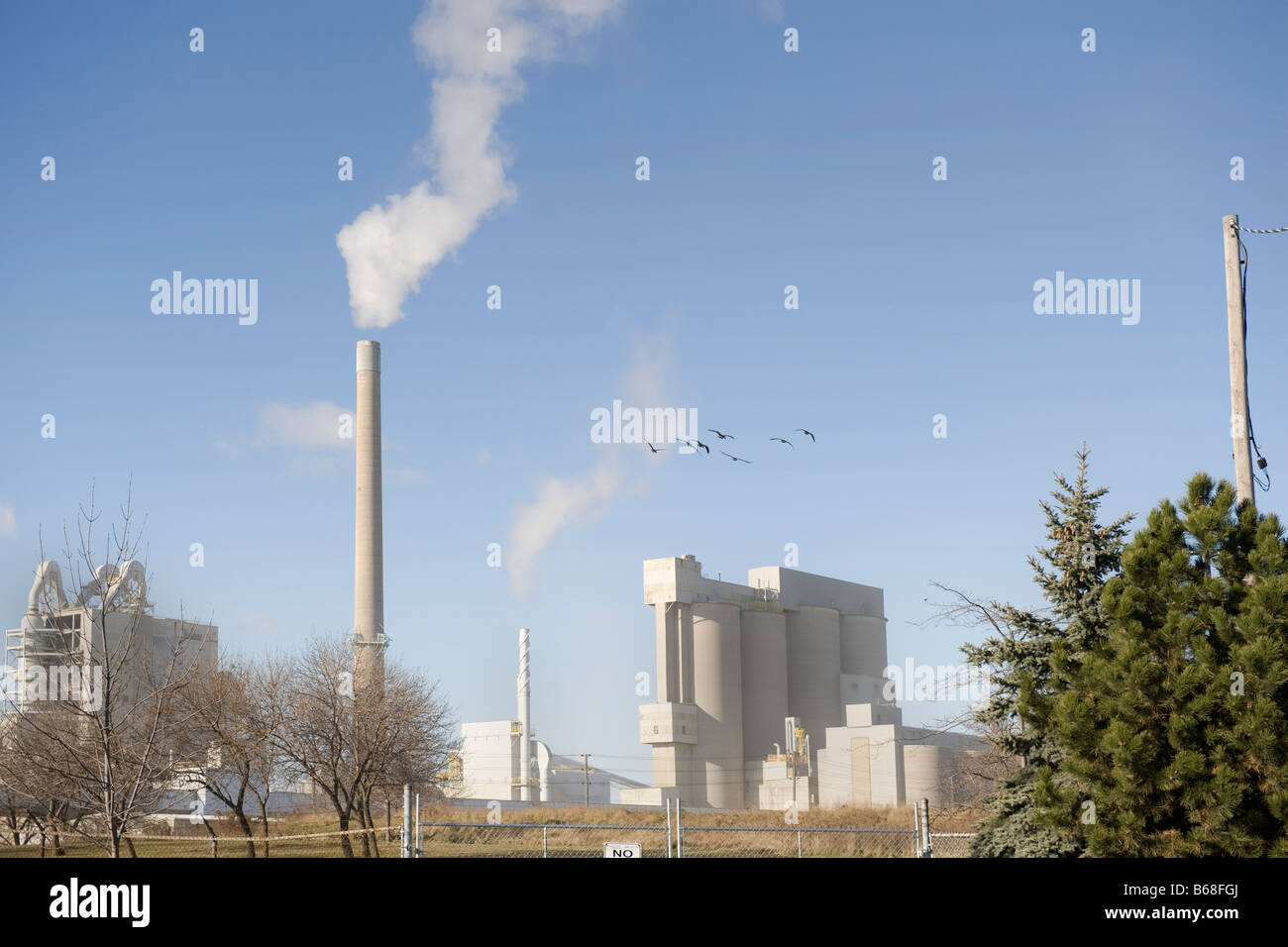 Cement factory with smoking chimney and wind blown dust in front of ...