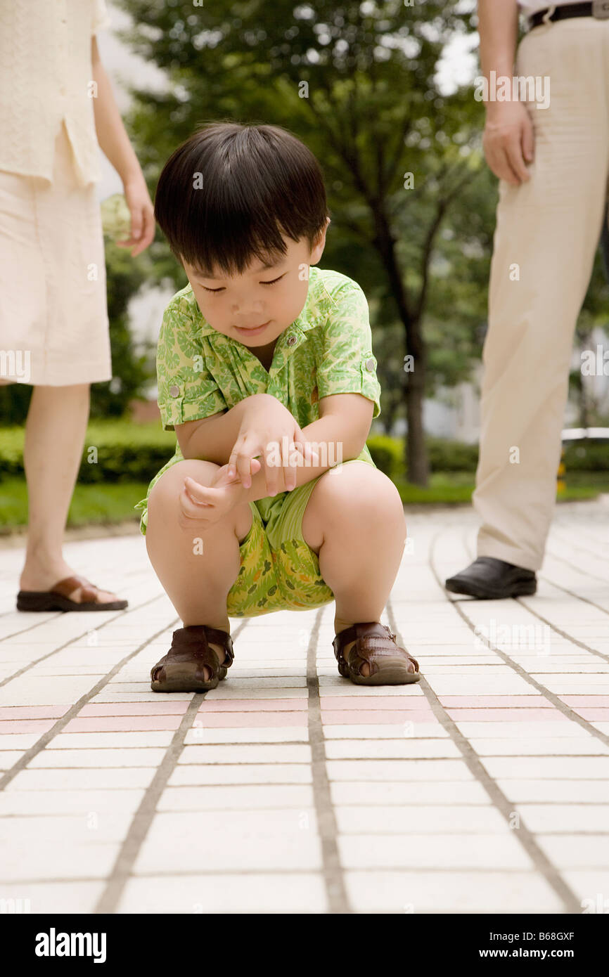 Boy crouching on a footpath with his grandparents standing behind him ...