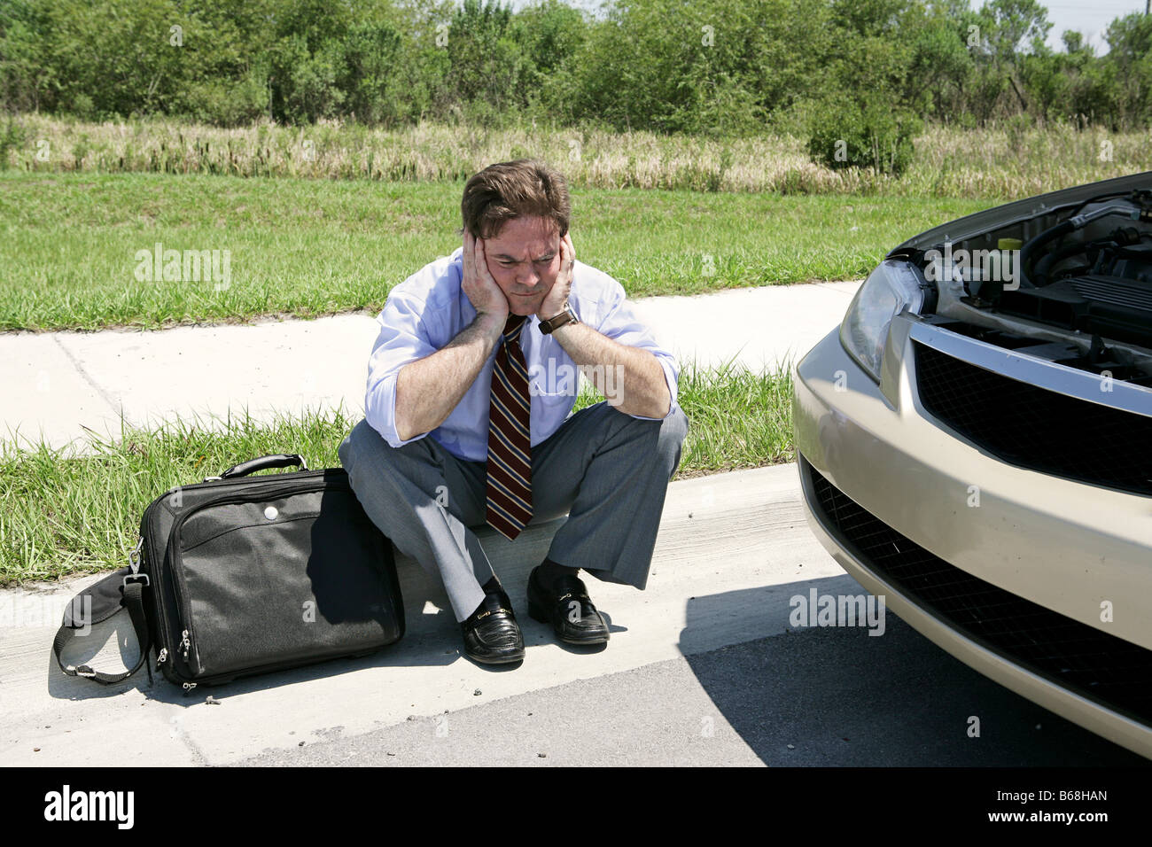 An upset businessman on the side of the road with his broken down car ...