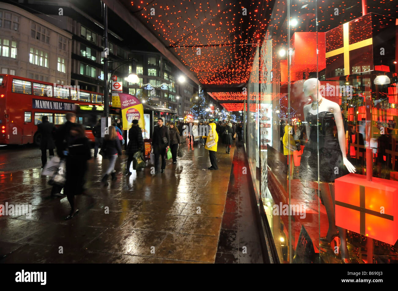 Shoppers on wet pavement outside department store front windows with ...