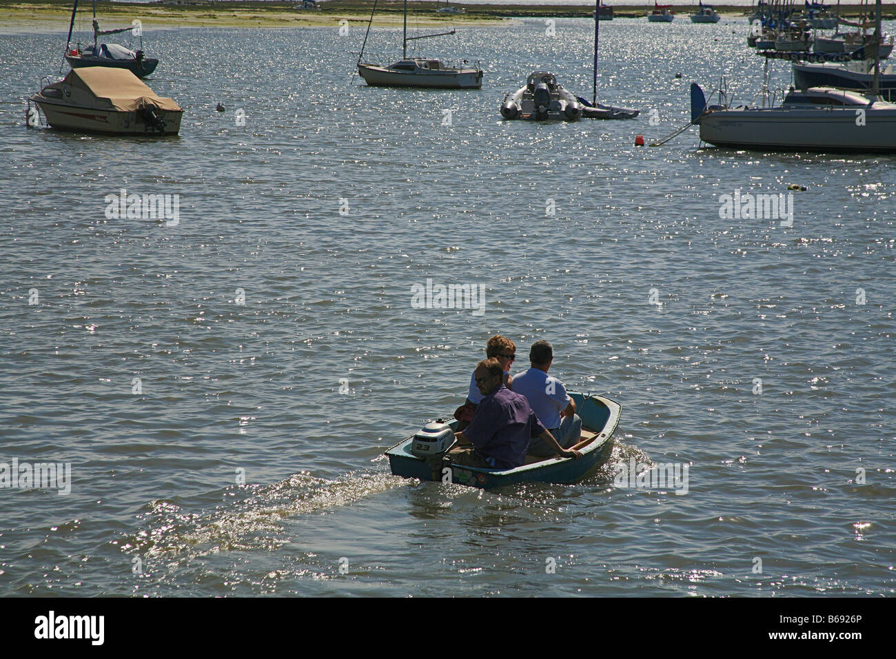 Three people in small dingy with outboard motor in Keyhaven harbour ...