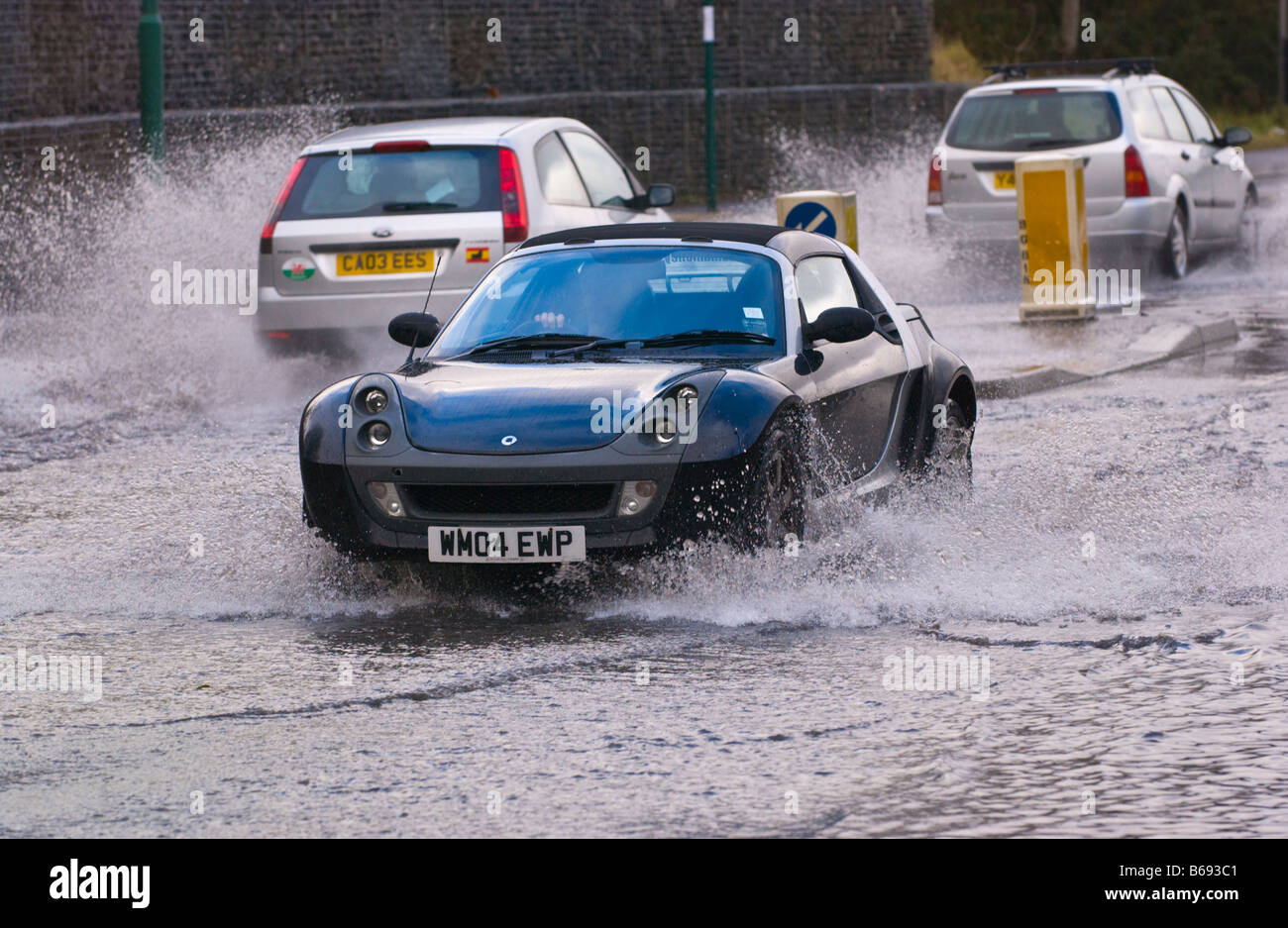 Cars drive through flood water splash after road flooded by heavy rain ...
