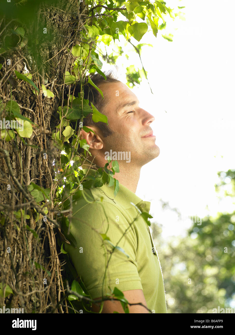 Young man leaning against tree Stock Photo - Alamy
