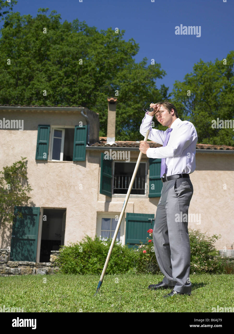 Suited man raking lawn Stock Photo - Alamy