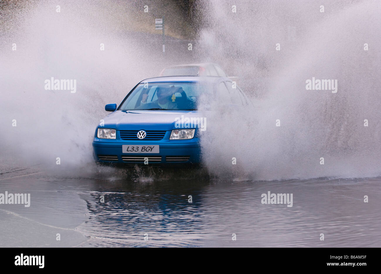 Cars drive through flood water splash after road flooded by heavy rain ...
