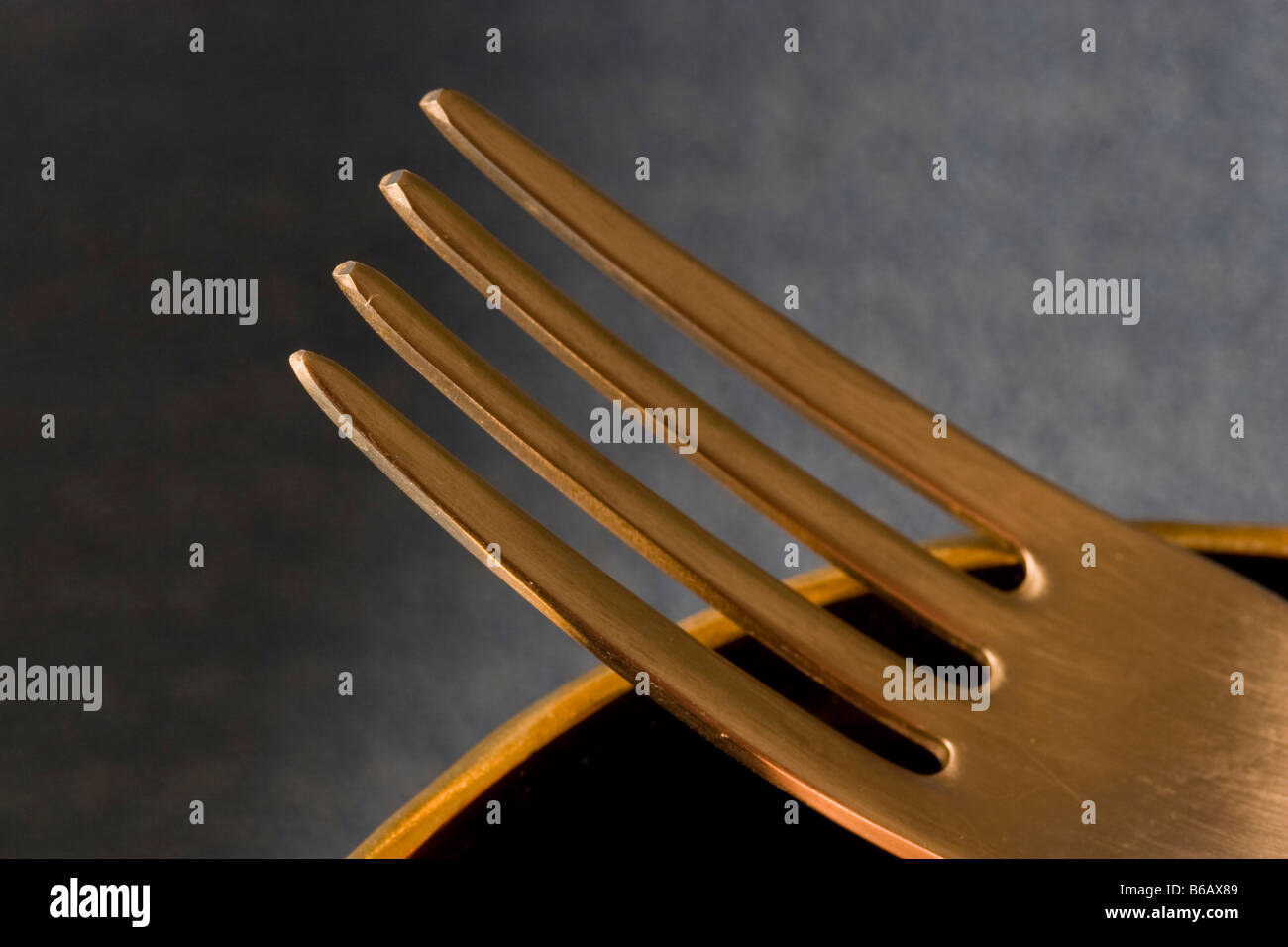 Macro golden fork bathed in golden light upon a Chinese bowl with blue ...