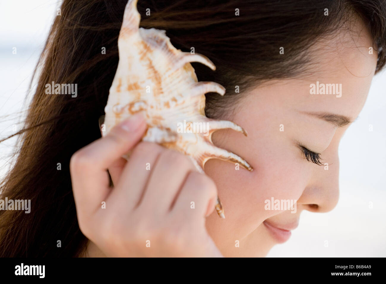 Young woman listening to seashell Stock Photo - Alamy