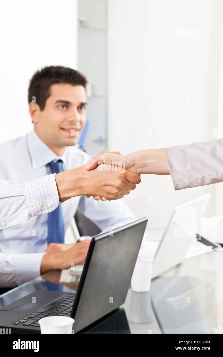 Businessman And Woman Shaking Hands In Office With Colleague Watching