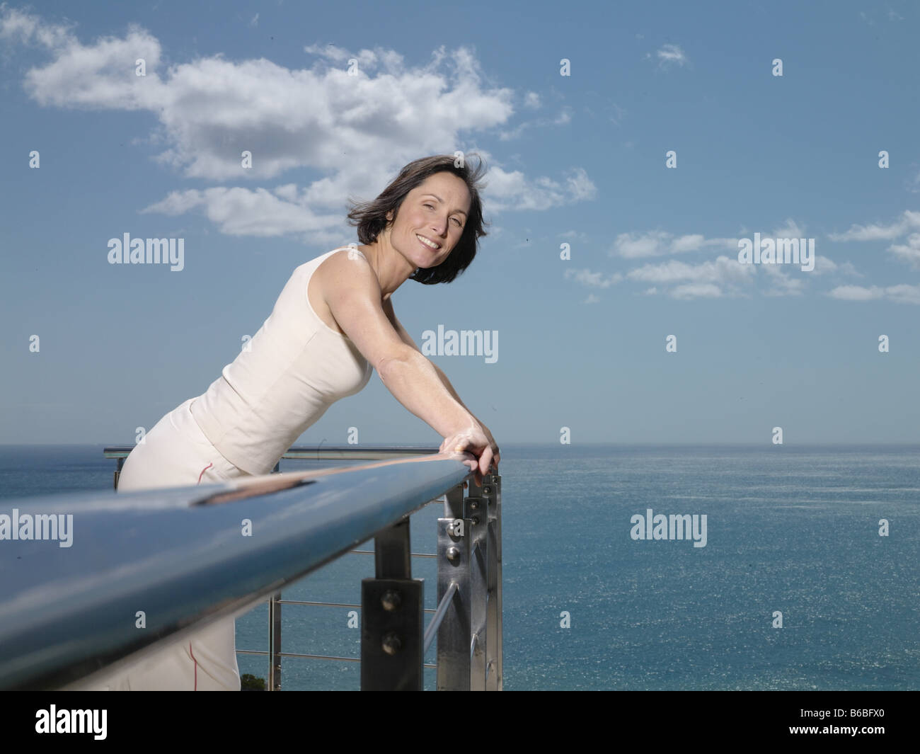 Portrait of woman leaning on railing and smiling Stock Photo - Alamy