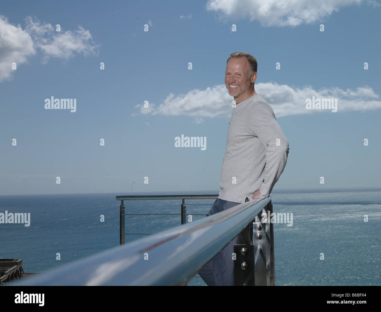 Portrait of man leaning against railing and smiling Stock Photo - Alamy