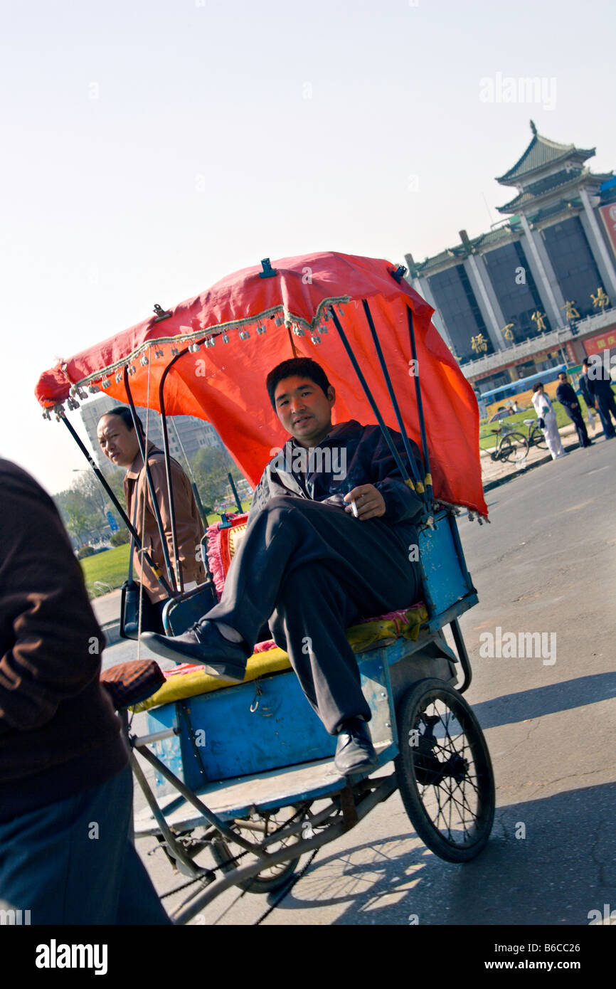 CHINA BEIJING Chinese man riding in a bright red bicycle rickshaw in ...