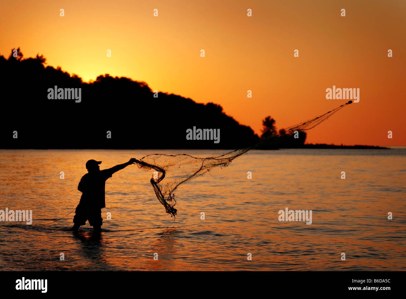A man casting a net into the ocean at sunset Stock Photo - Alamy