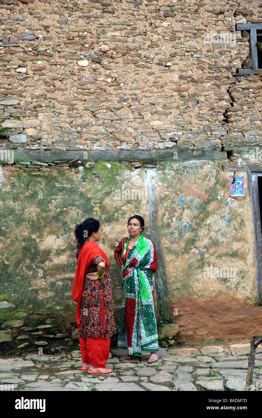 Two women gossip by the crumbling wall of an old house, Dolakha ...