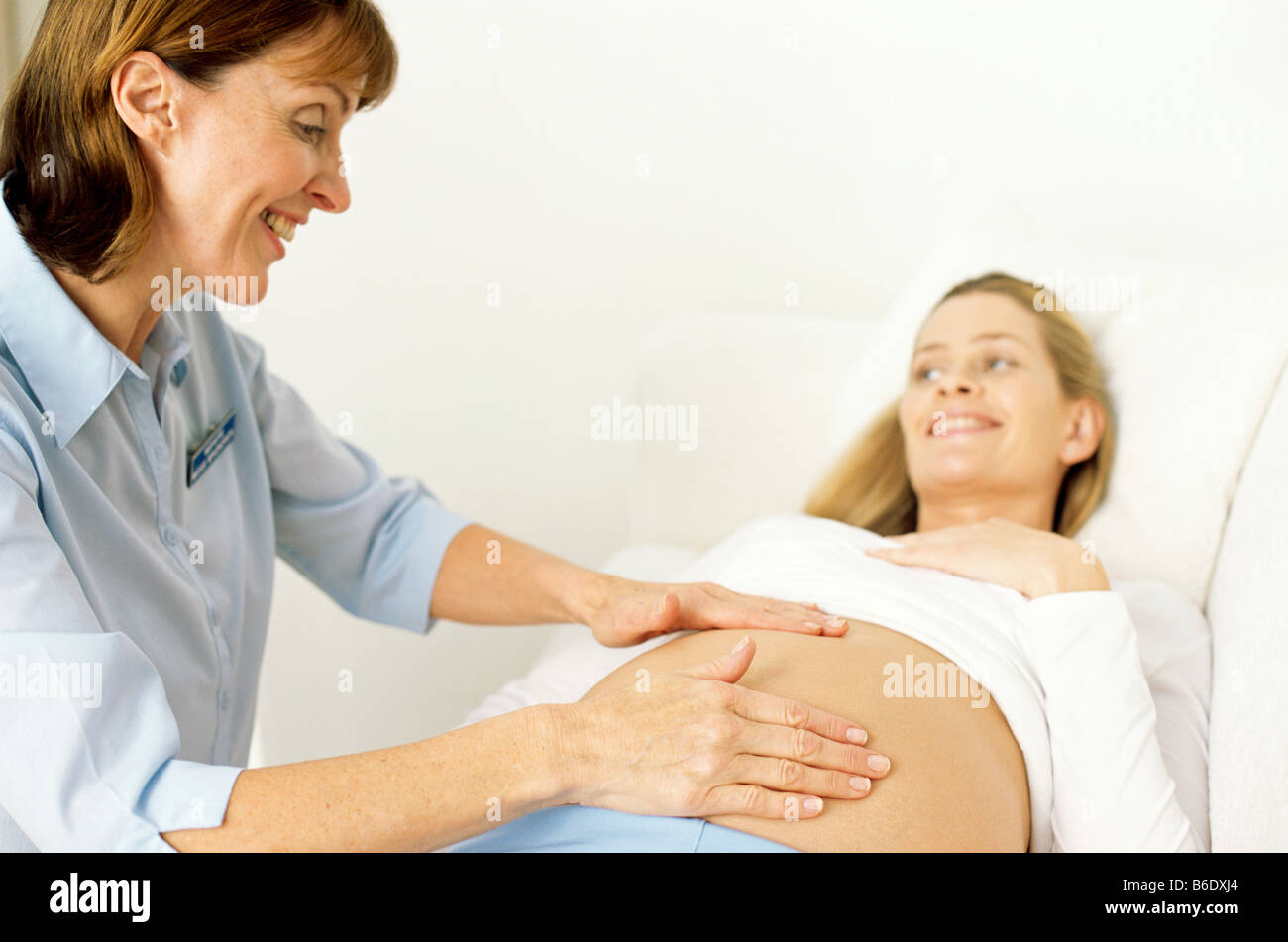 Obstetric examination. Midwide palpating a pregnant woman's abdomen to ...