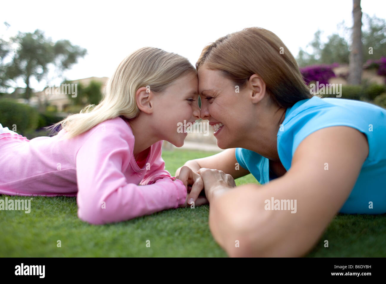 Smiling mother and daughter touching faces as they lie on the ground ...