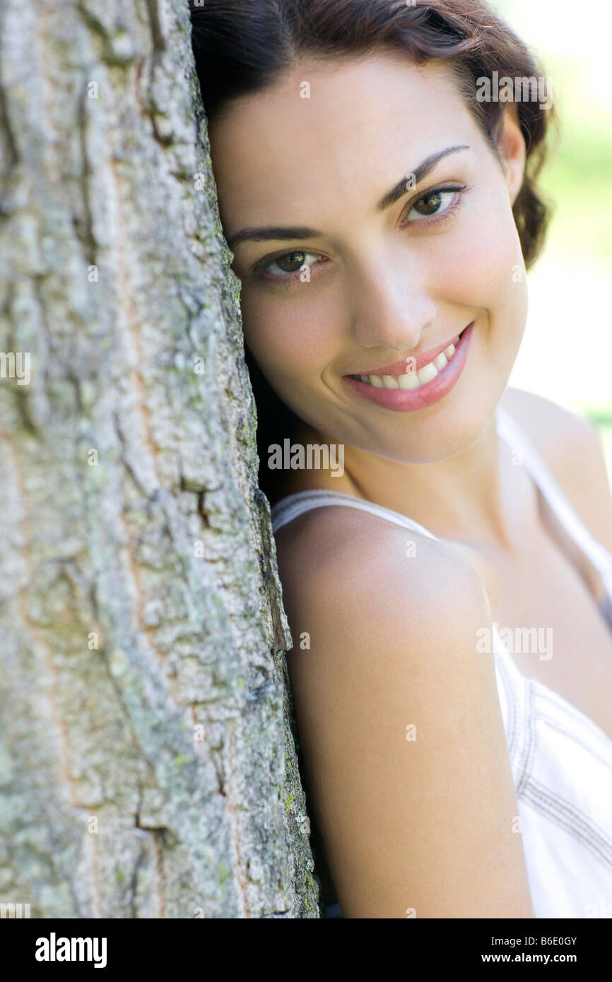 Happy woman leaning against tree Stock Photo - Alamy