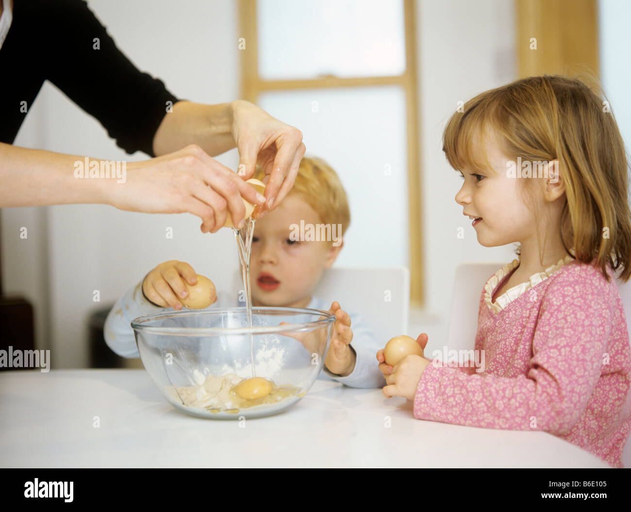 Making cakes. Two three year old children watch their mother breaking ...