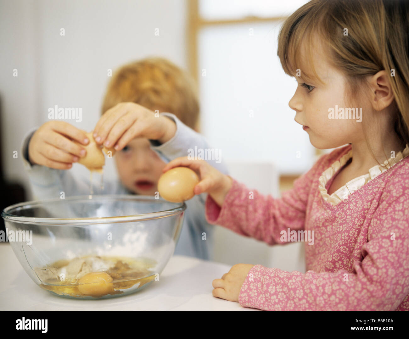 Making cakes. Two three year old children cracking eggs on the side of ...